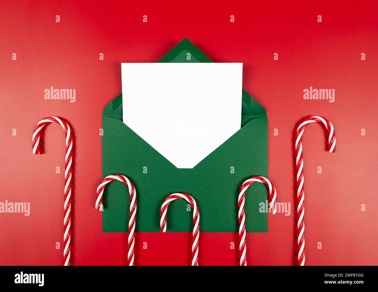 Top view of green envelope, white card and candy canes on red ...