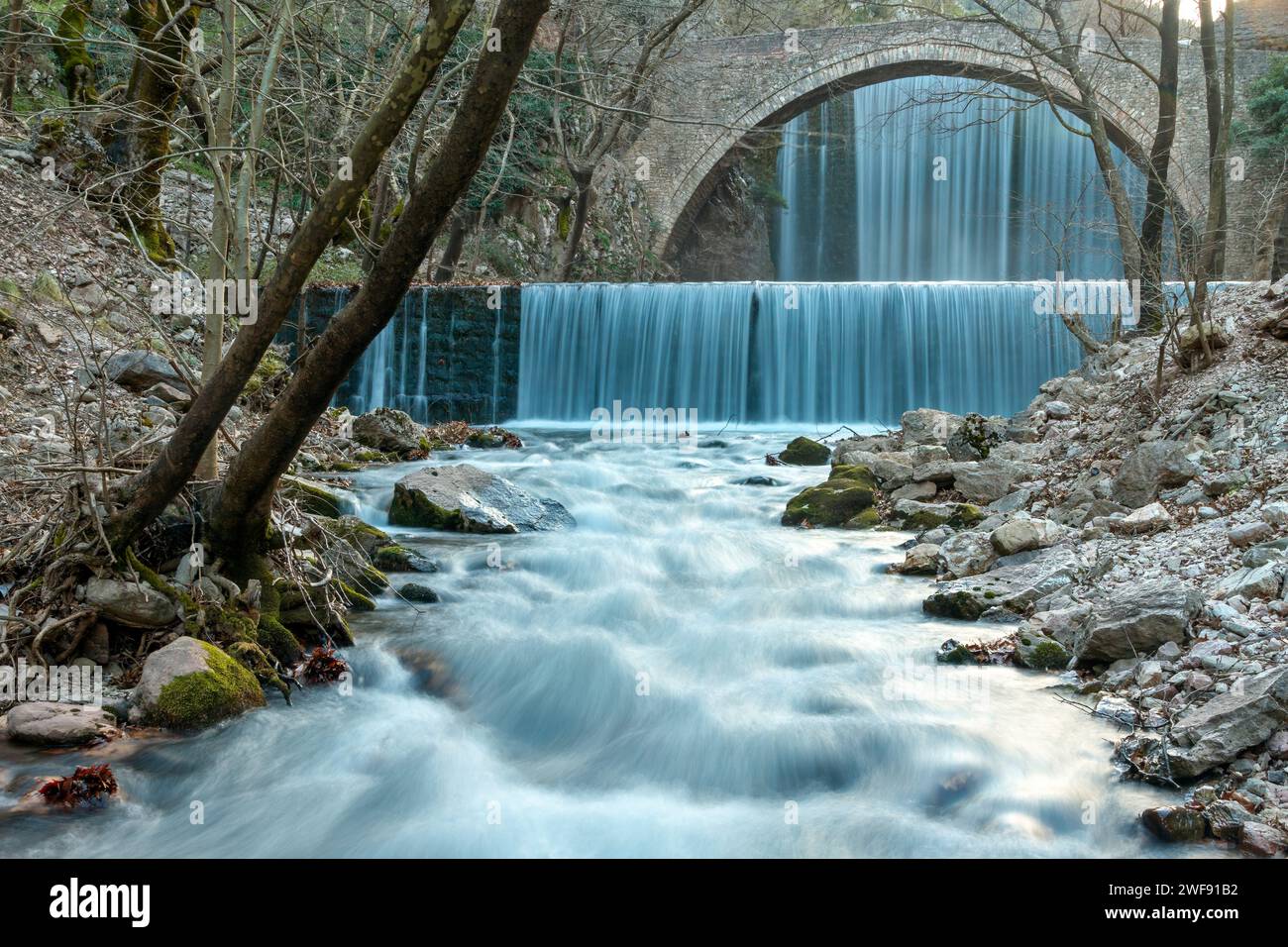 An old stone bridge with large arch, between two waterfalls in ...