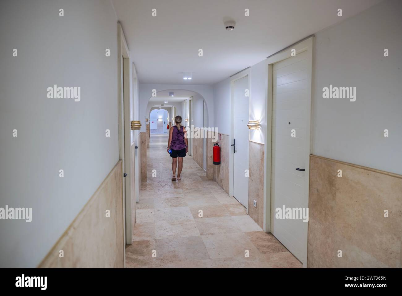Beautiful hotel interior featuring a long corridor, where a woman walks ...