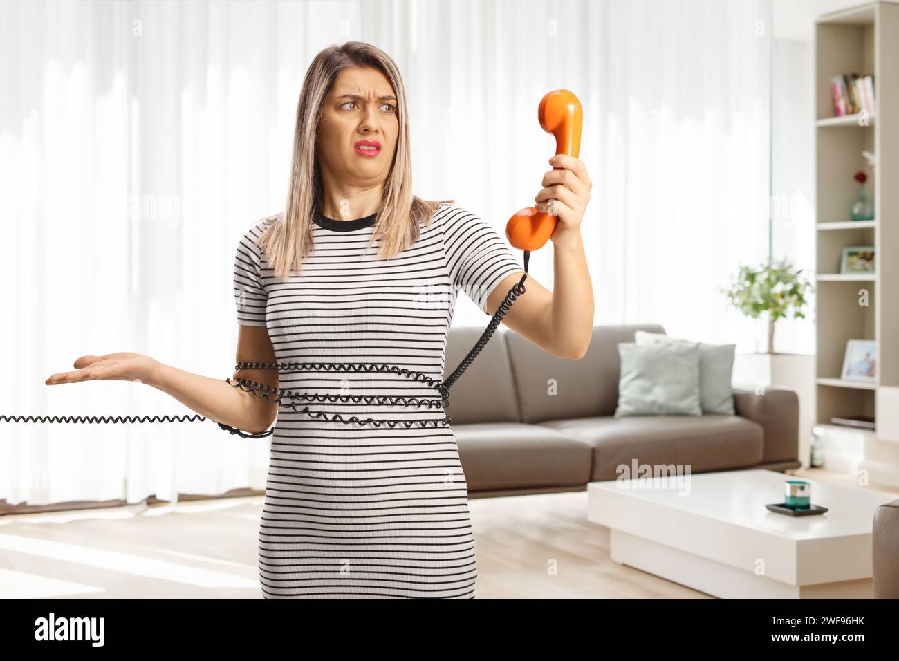 Angry woman tangled with a cable from a vintage rotary phone looking at ...