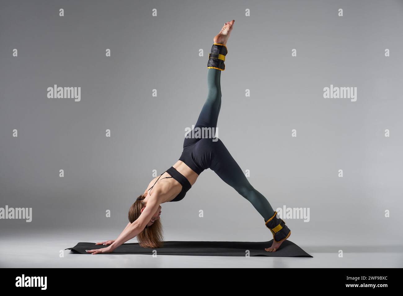 Slim woman practicing yoga, while raising one leg in studio. Side view ...