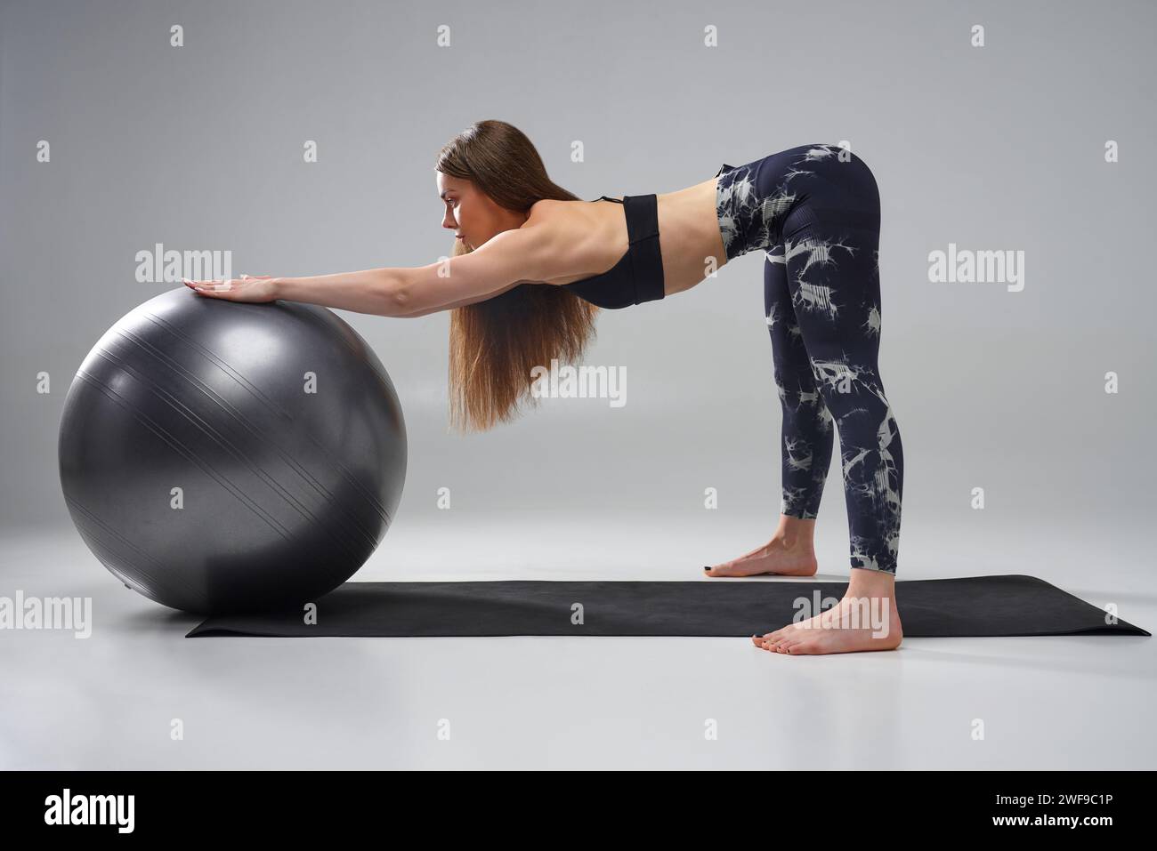 Slim, flexible woman in sportswear, exercising on big fit ball indoors ...