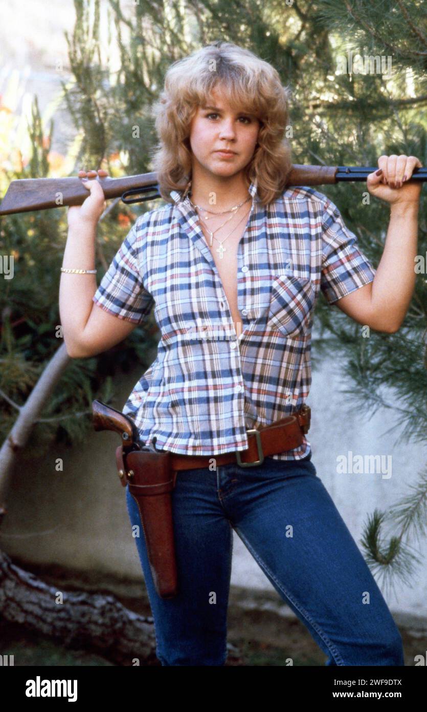 Linda Blair in flannel shirt unbuttoned, holding gun behind her head, wearing holster, on set of ...