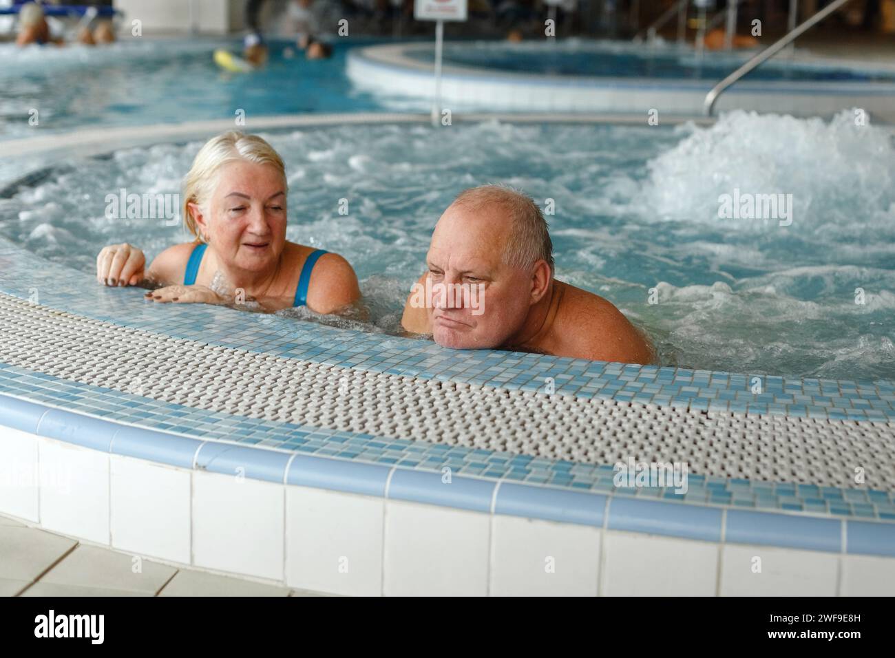 Happy elderly couple enjoying hydromassage in the swimming pool at the ...