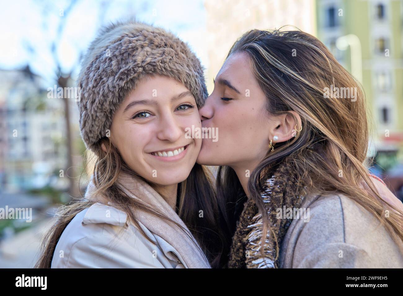 Affectionate girl kissing to her happy friend on the street in winter ...