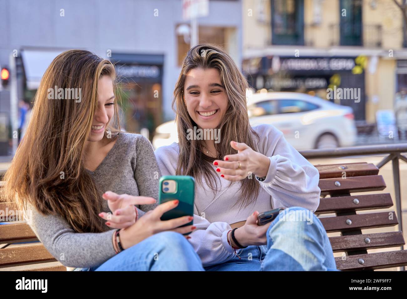 two women laughing while looking at their cell phones sitting on a city ...