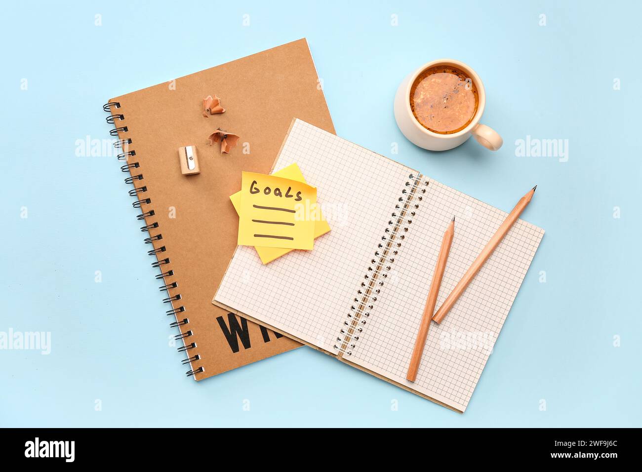 Sticky note with word GOALS, notebooks and cup of coffee on blue ...