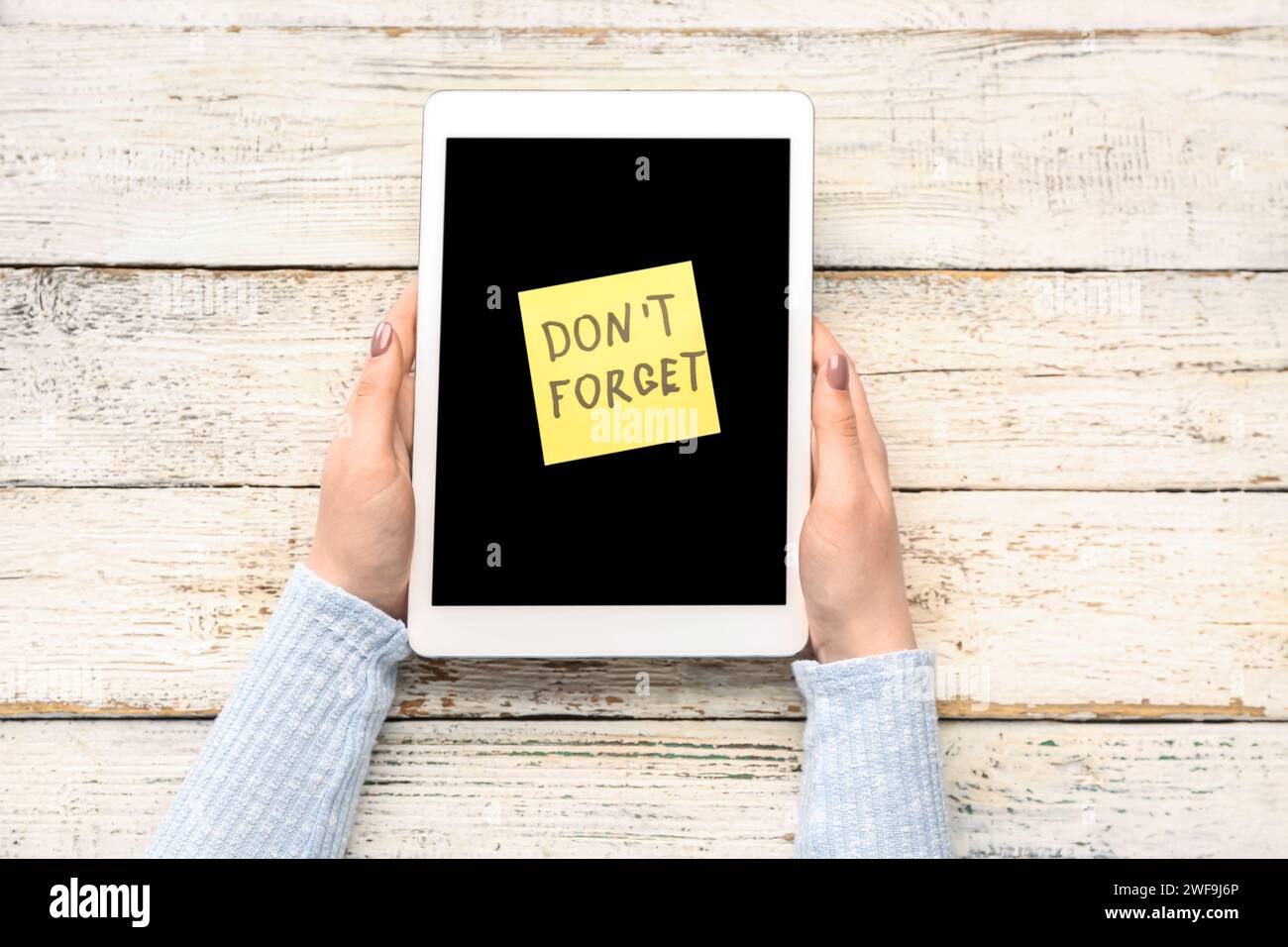 Sticky note with text DON'T FORGET and tablet computer on white wooden ...