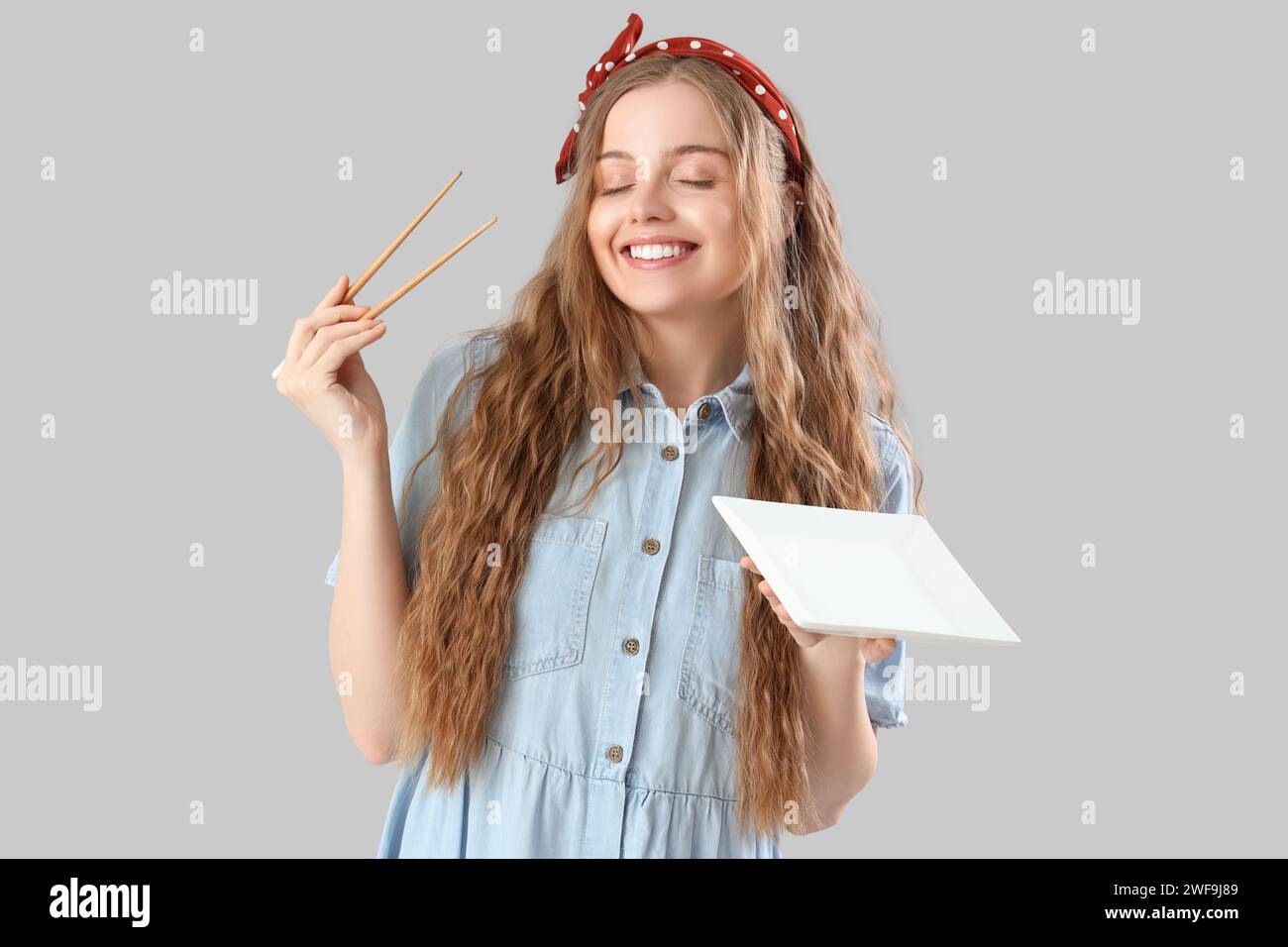 Beautiful young woman with empty plate and chopsticks on grey ...