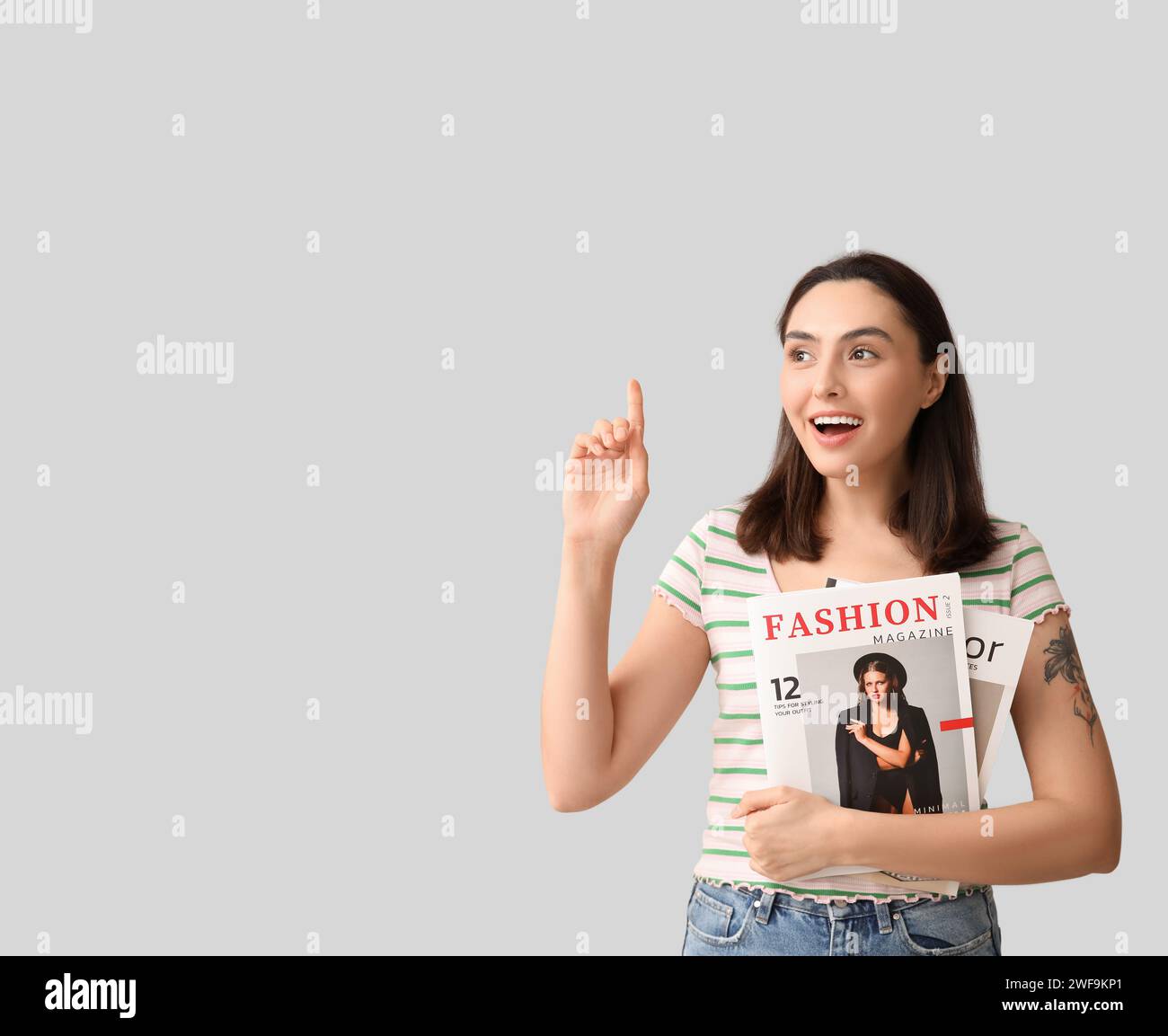 Beautiful woman with magazines pointing at something on light ...