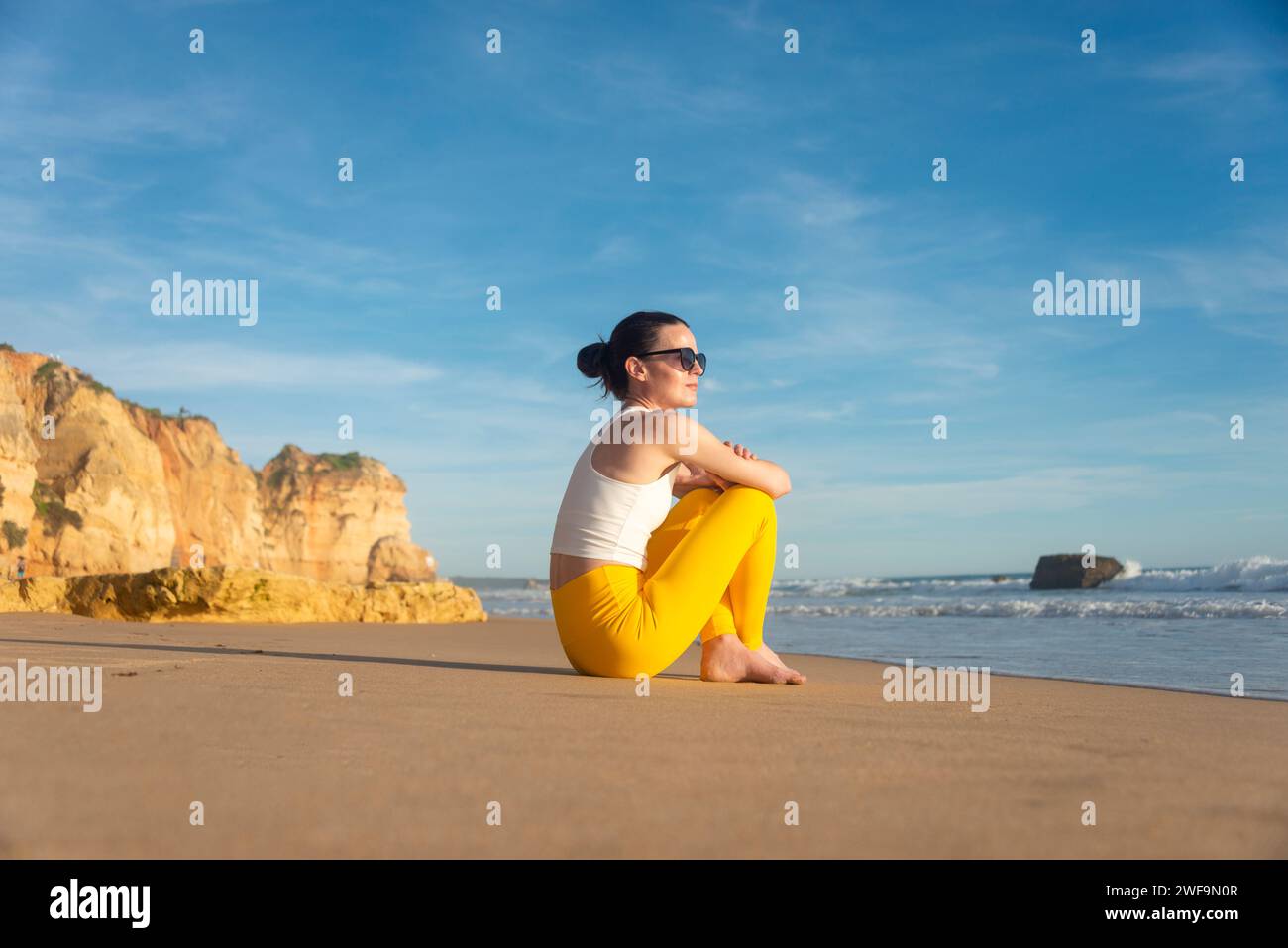 sporty woman sitting on the beach in the sun resting Stock Photo - Alamy