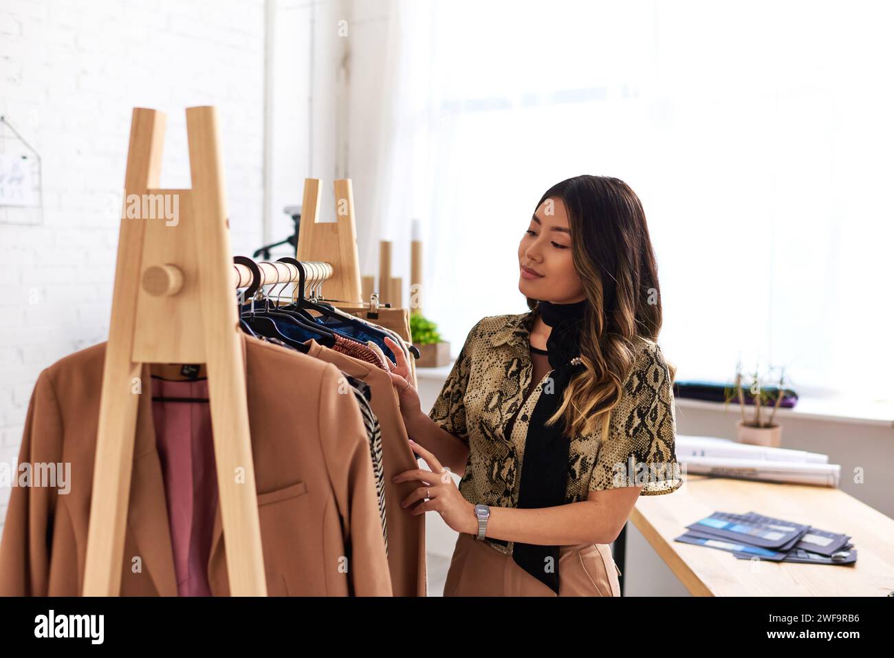 young creative asian designer looking at fashionable bespoke garments ...