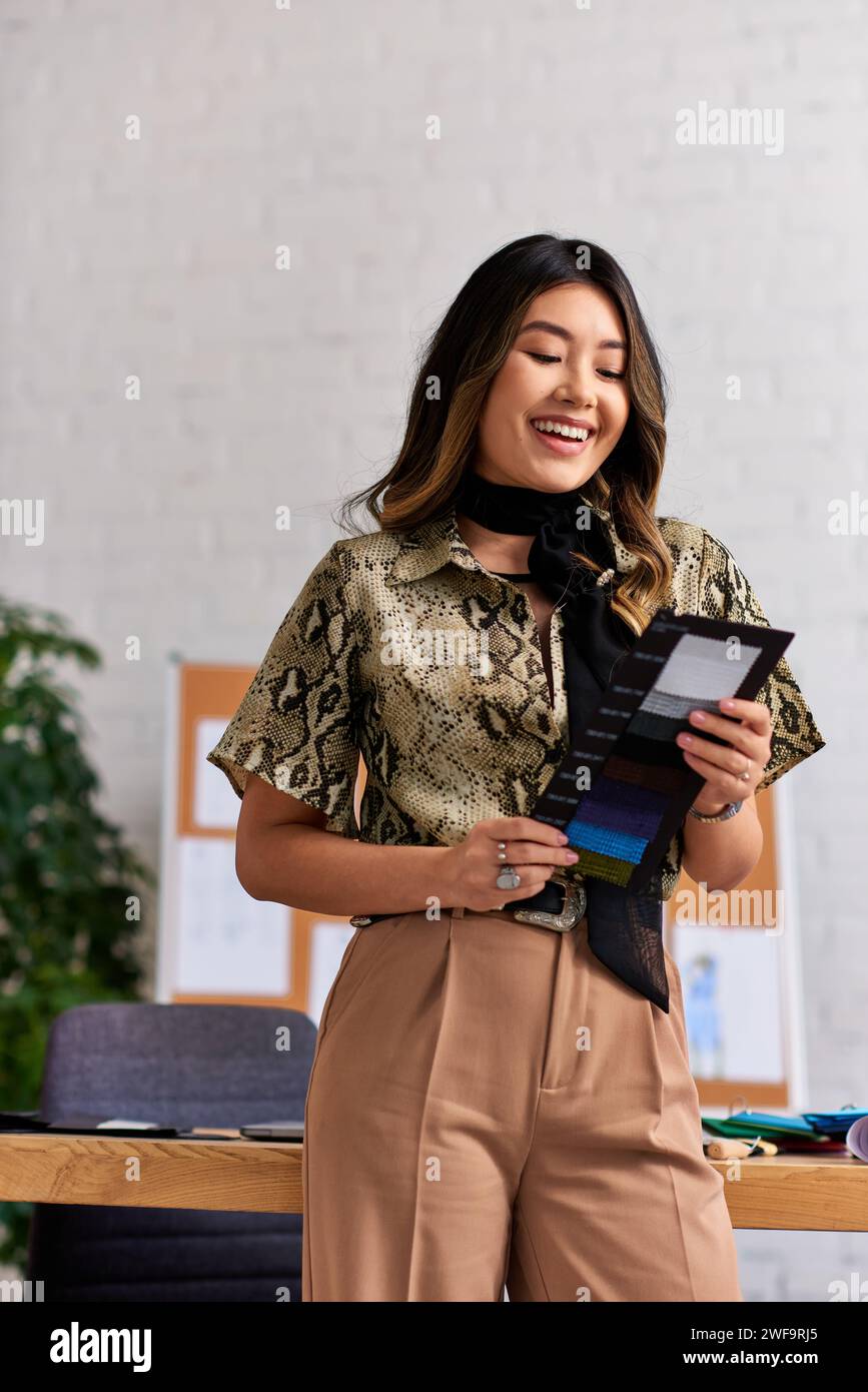 pleased and trendy asian clothes designer looking at color swatches in ...