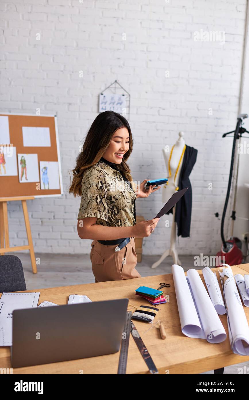 inspired asian stylist looking at color swatches near laptop and sewing ...