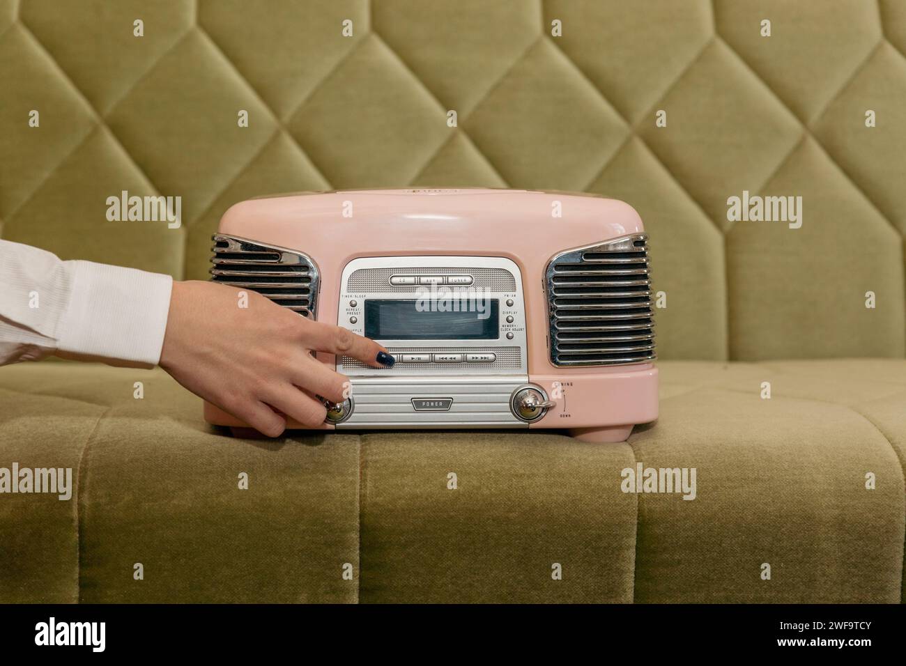 A close-up of a woman's hand pressing buttons on a vintage pink radio ...