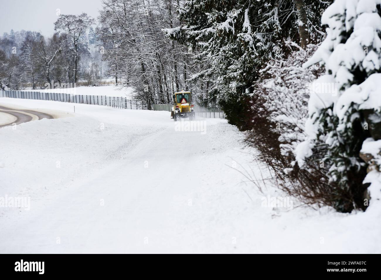 A powerful tractor braves the frozen landscape, its snowplow clearing a ...