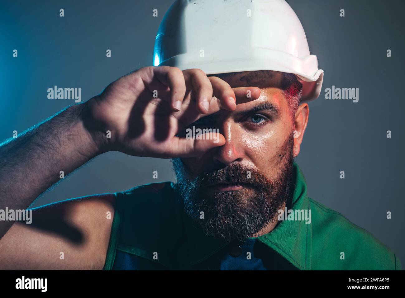 Closeup portrait of tired builder in construction helmet. Fatigued worker wipes sweat from ...