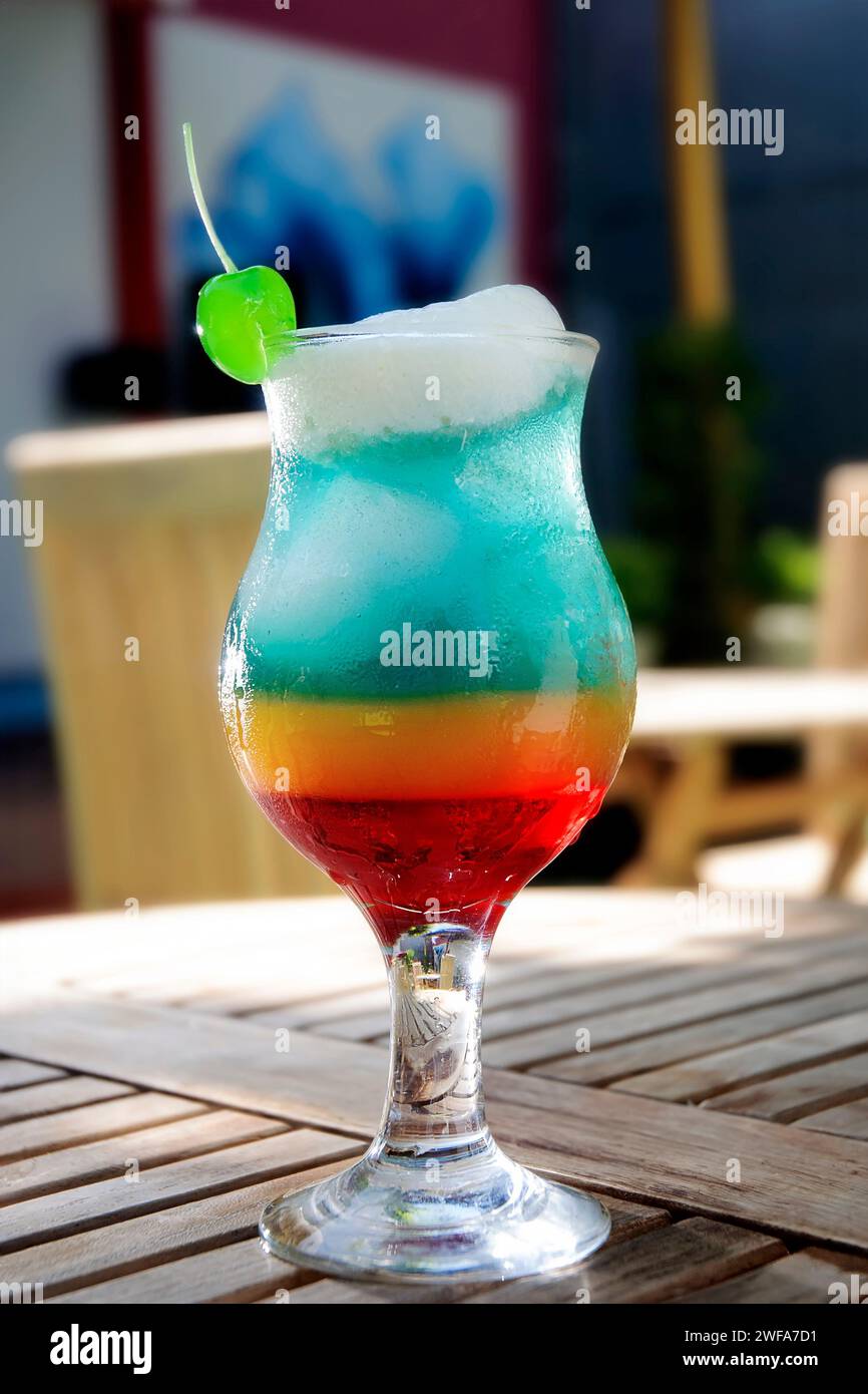 a glass of rainbow mocktail served with ice and a cherry as decoration ...