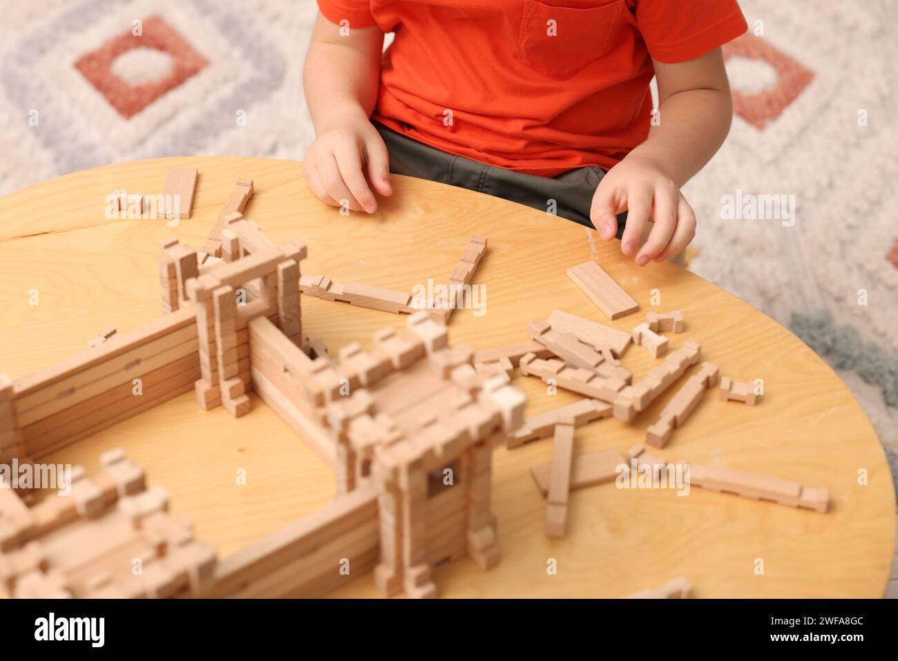 Little boy playing with wooden construction set at table in room ...