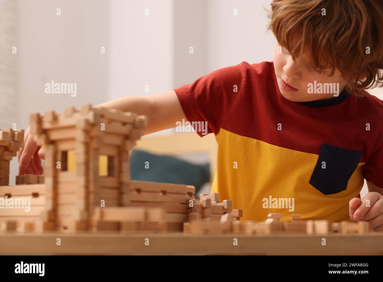 Little boy playing with wooden entry gate at table in room. Child's toy ...