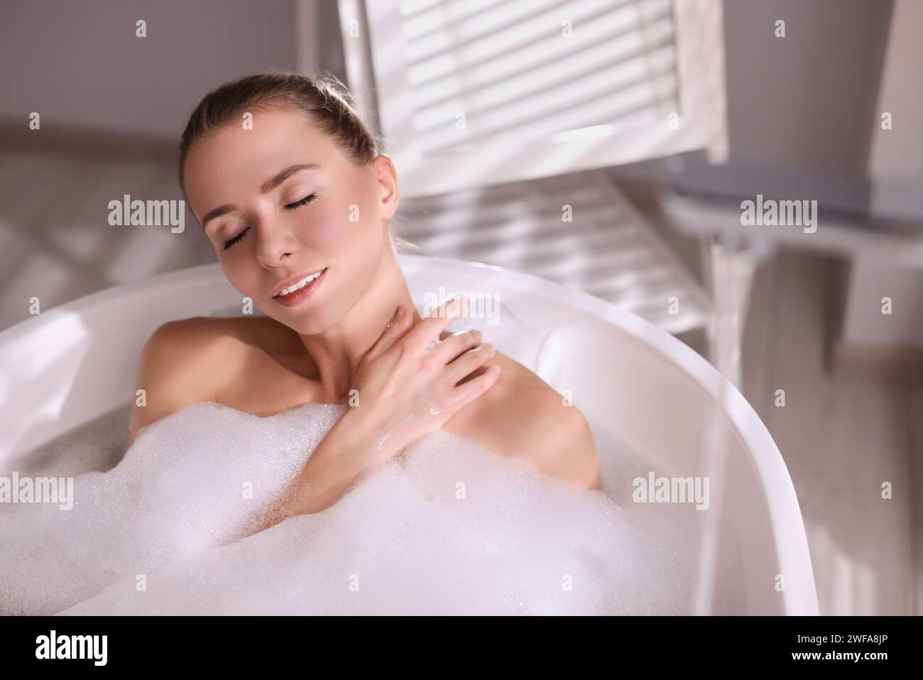 Beautiful woman taking bath in tub with foam indoors. Space for text ...
