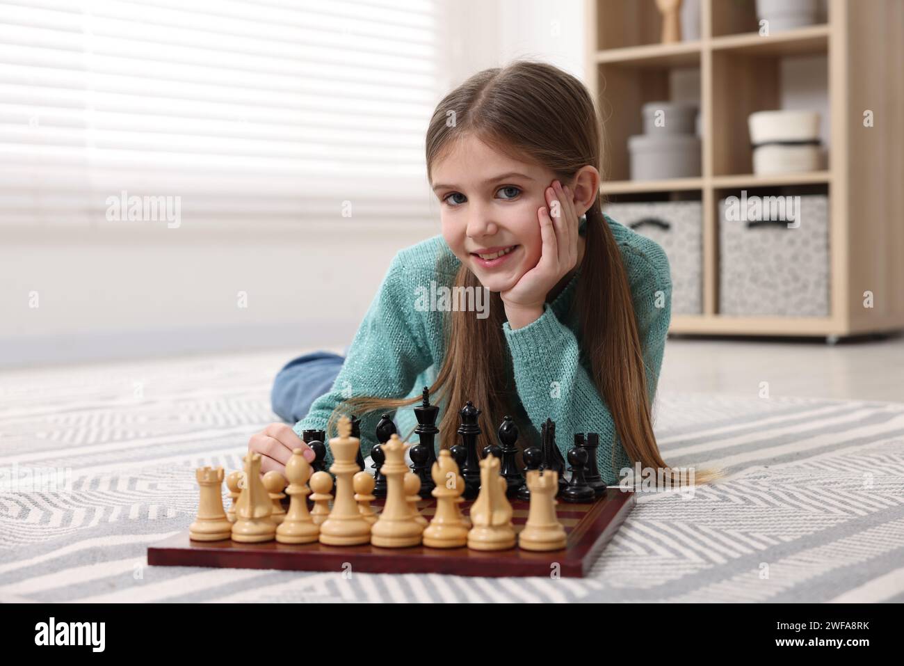 Cute girl playing chess on floor in room Stock Photo - Alamy