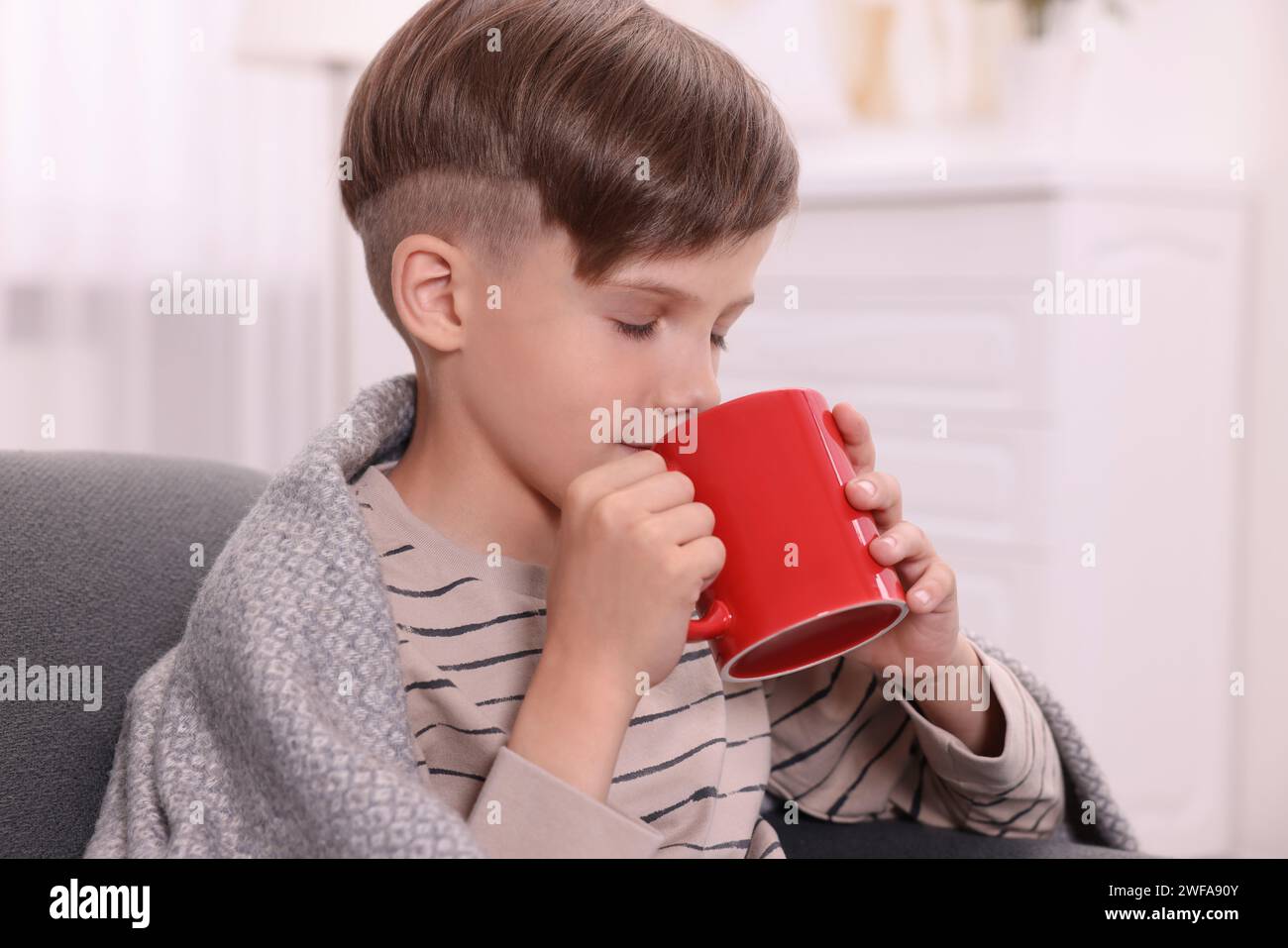 Cute boy drinking from red ceramic mug on sofa at home Stock Photo - Alamy