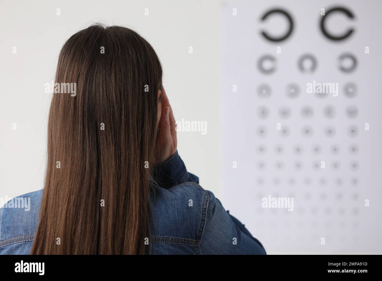 Eyesight examination. Young woman looking at vision test chart indoors ...