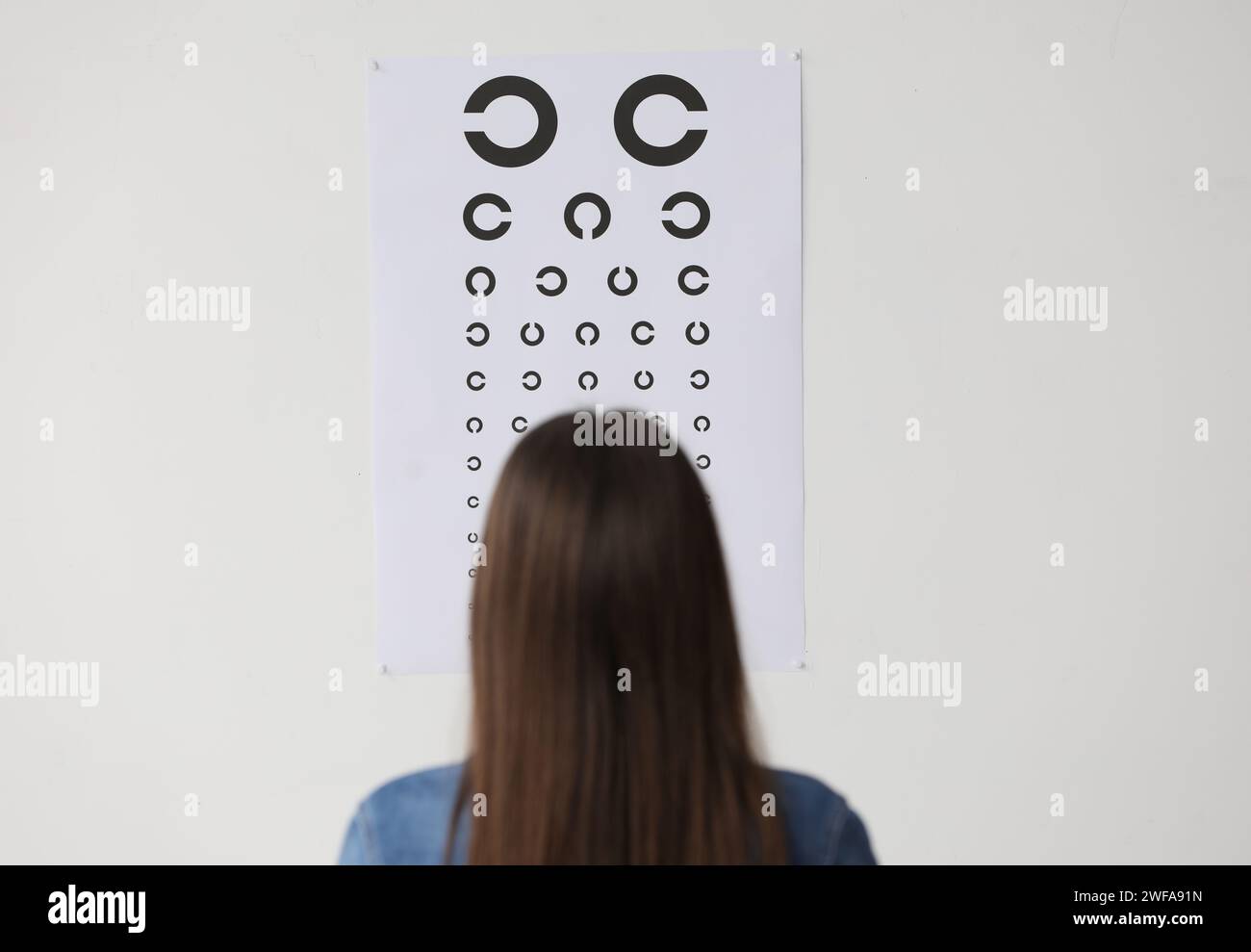Eyesight examination. Young woman looking at vision test chart indoors ...