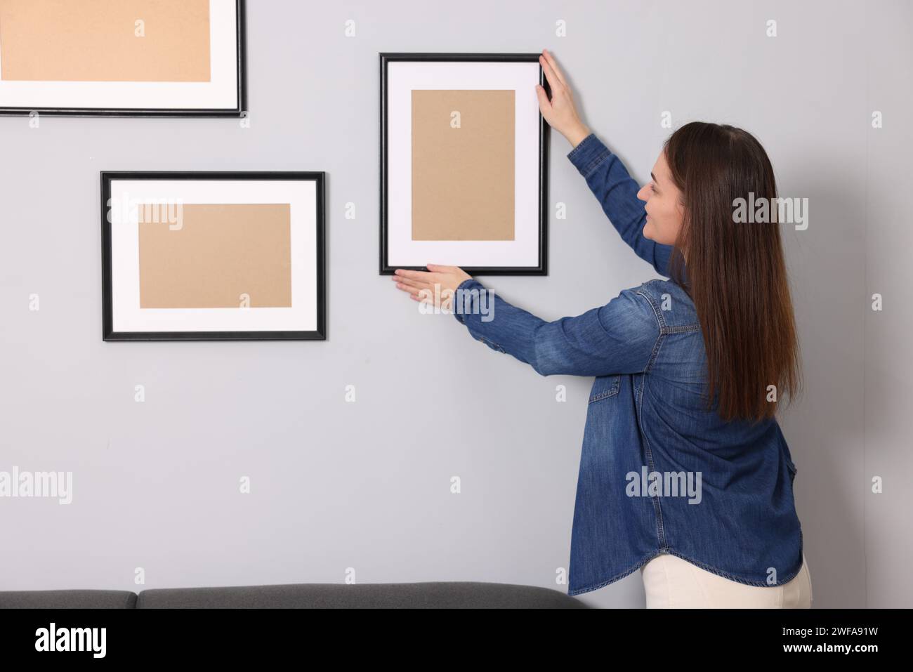 Woman hanging picture frame on gray wall Stock Photo - Alamy