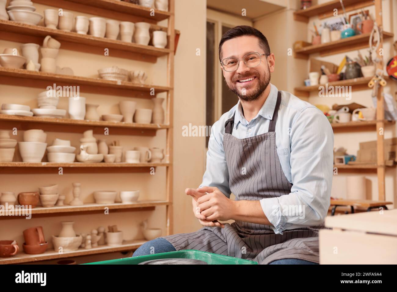 Happy man crafting with clay indoors. Different ceramics and potter's ...