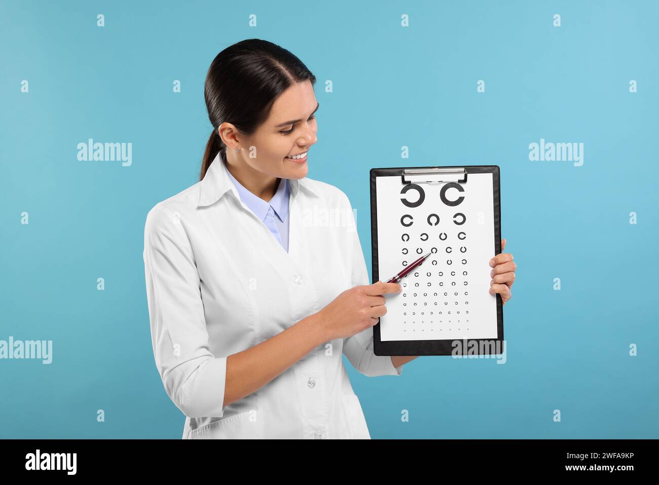 Ophthalmologist pointing at vision test chart on light blue background ...