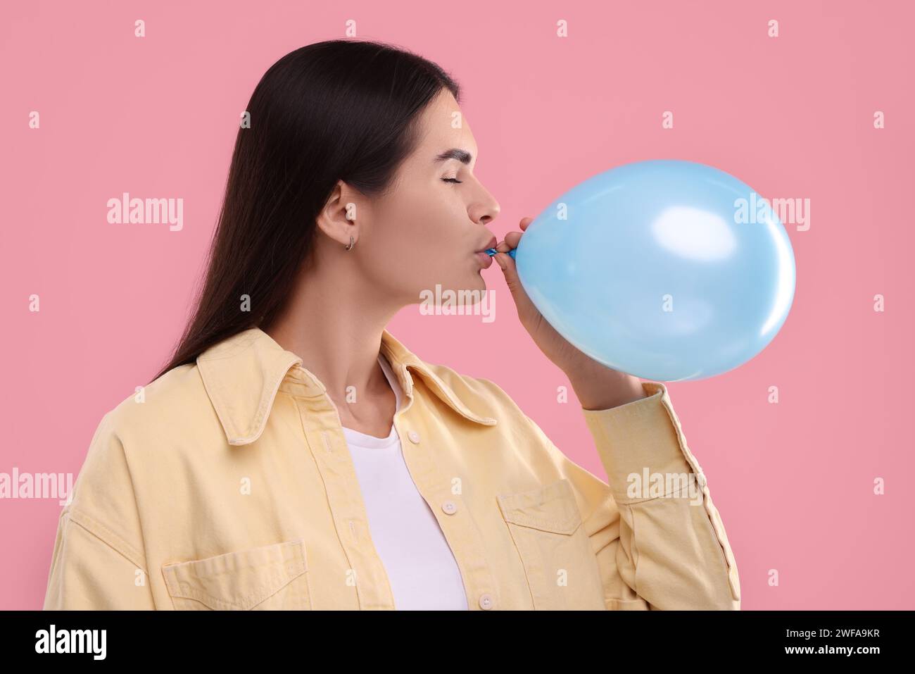 Woman inflating light blue balloon on pink background Stock Photo - Alamy