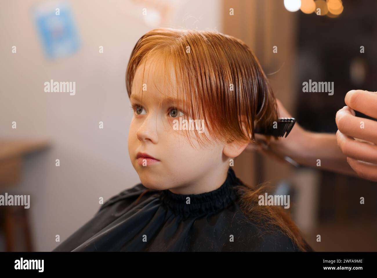 Professional hairdresser combing boy's hair in beauty salon, closeup ...