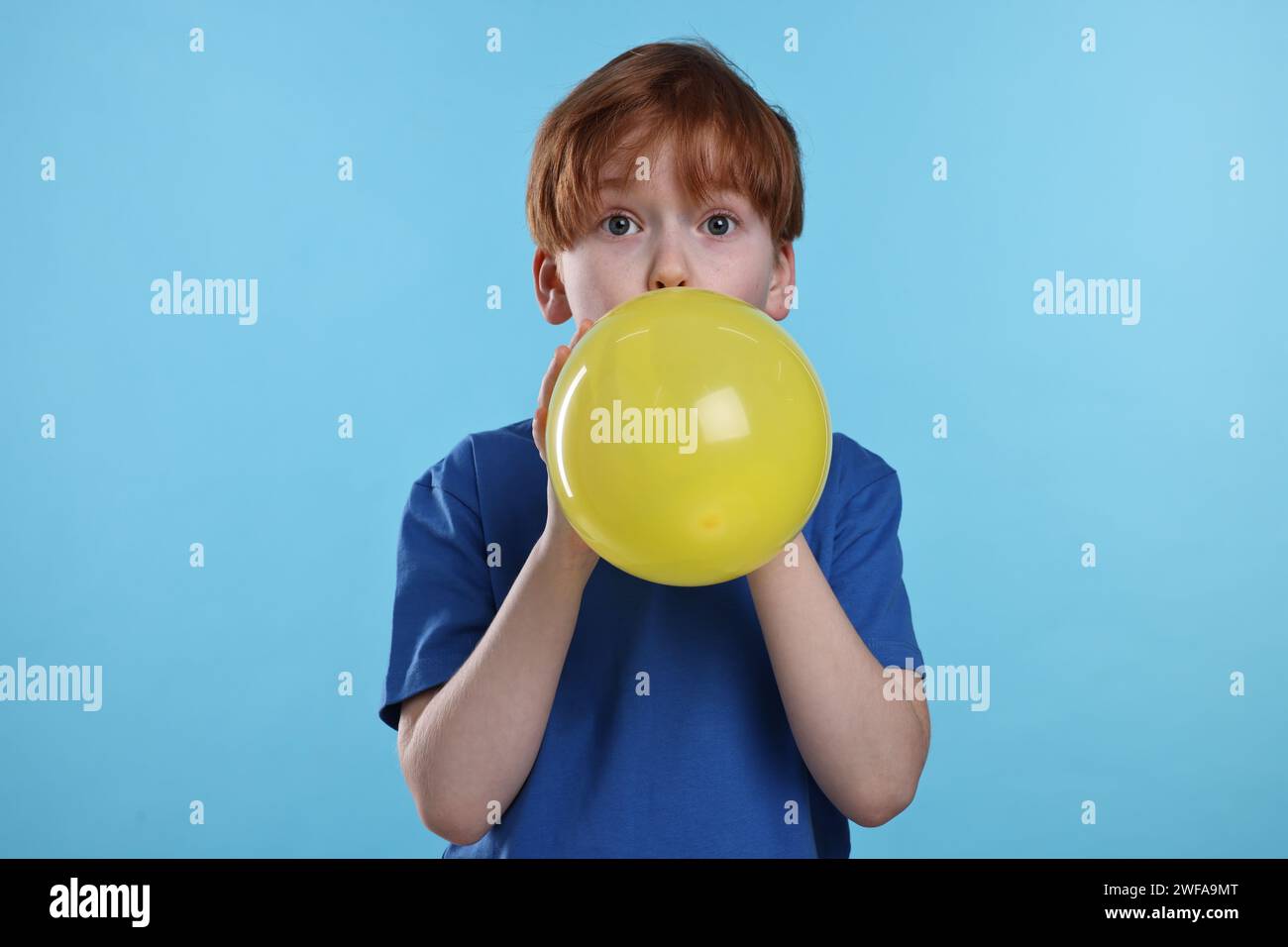 Boy inflating yellow balloon on light blue background Stock Photo - Alamy