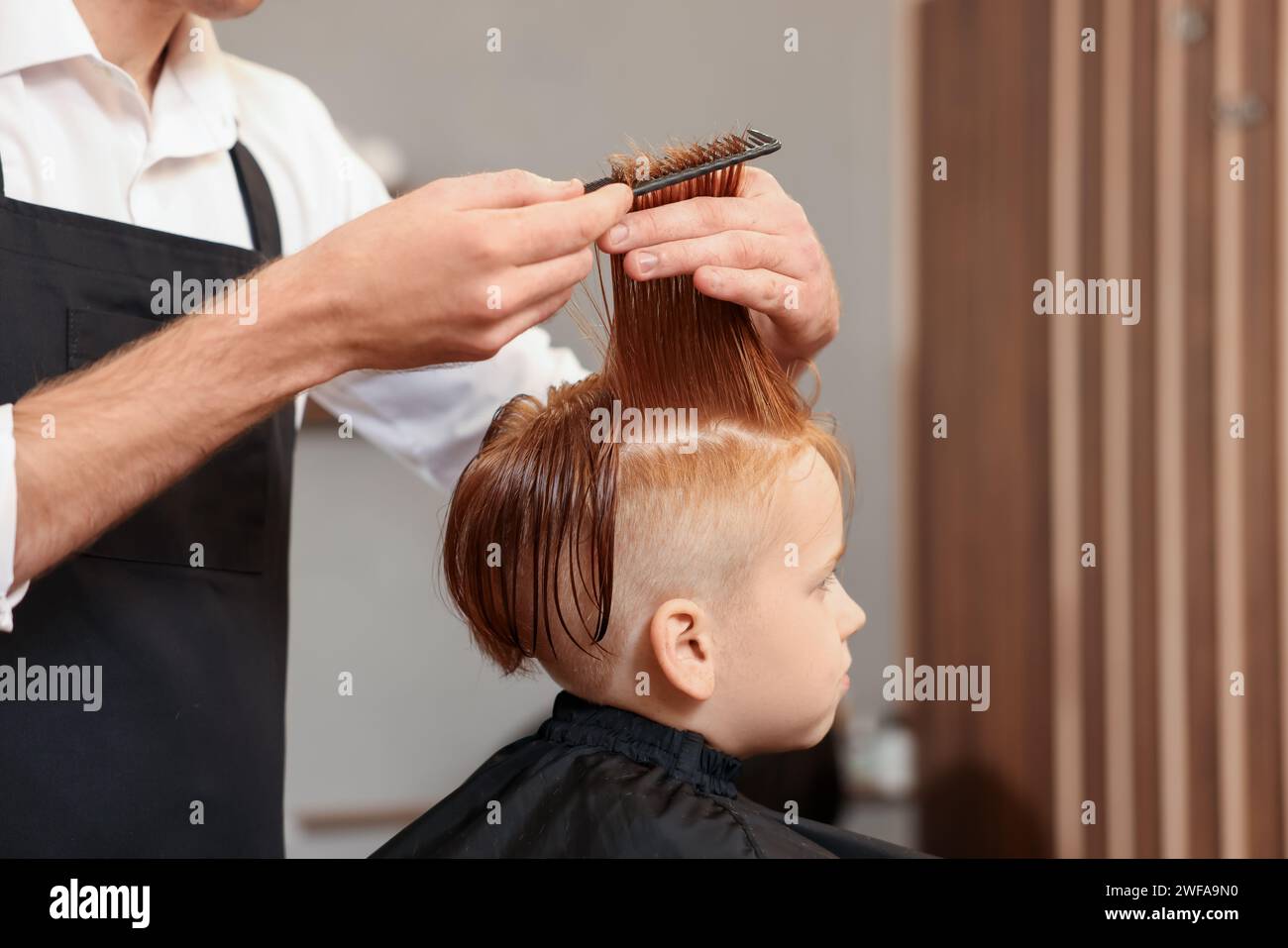 Professional hairdresser combing boy's hair in beauty salon, closeup ...