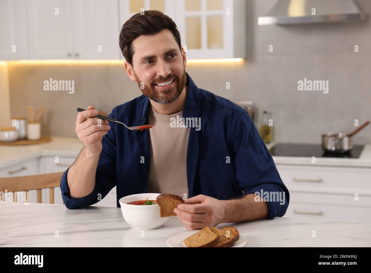 Man eating delicious tomato soup at light marble table in kitchen Stock ...