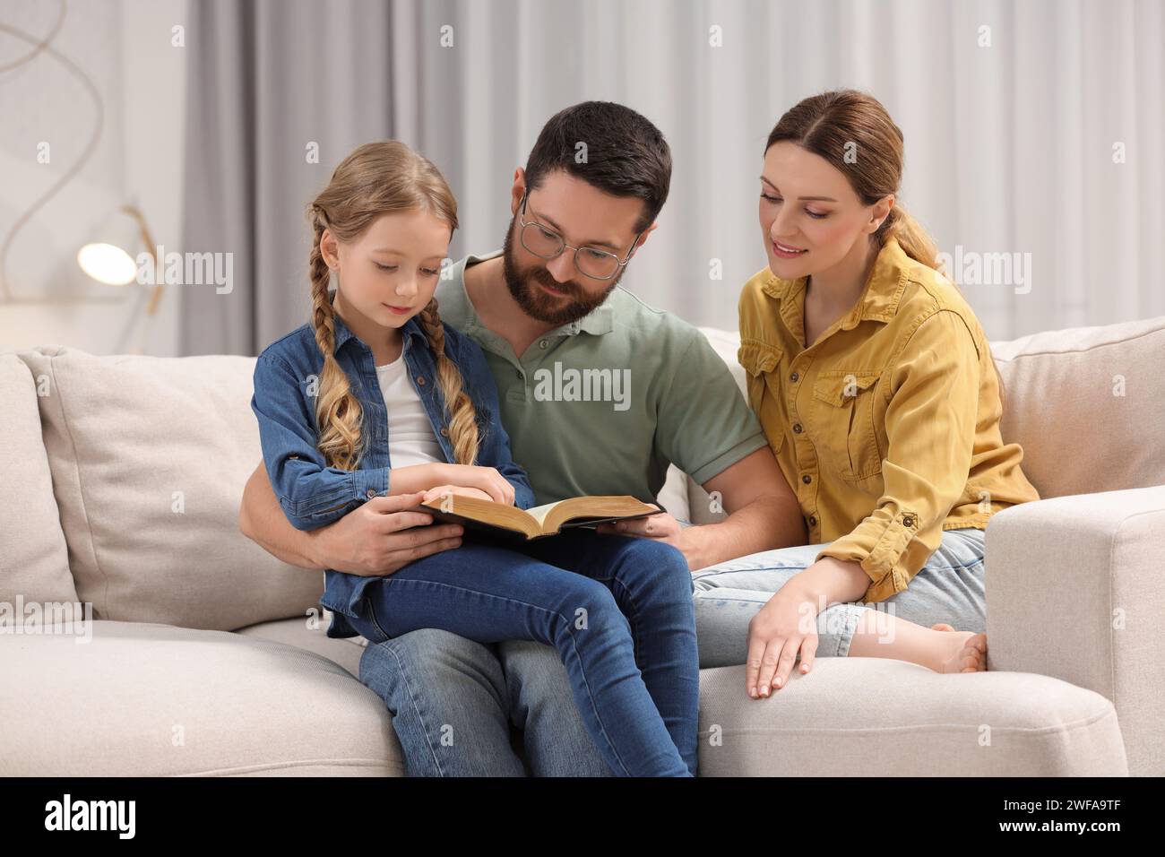 Girl and her godparents reading Bible together on sofa at home Stock ...