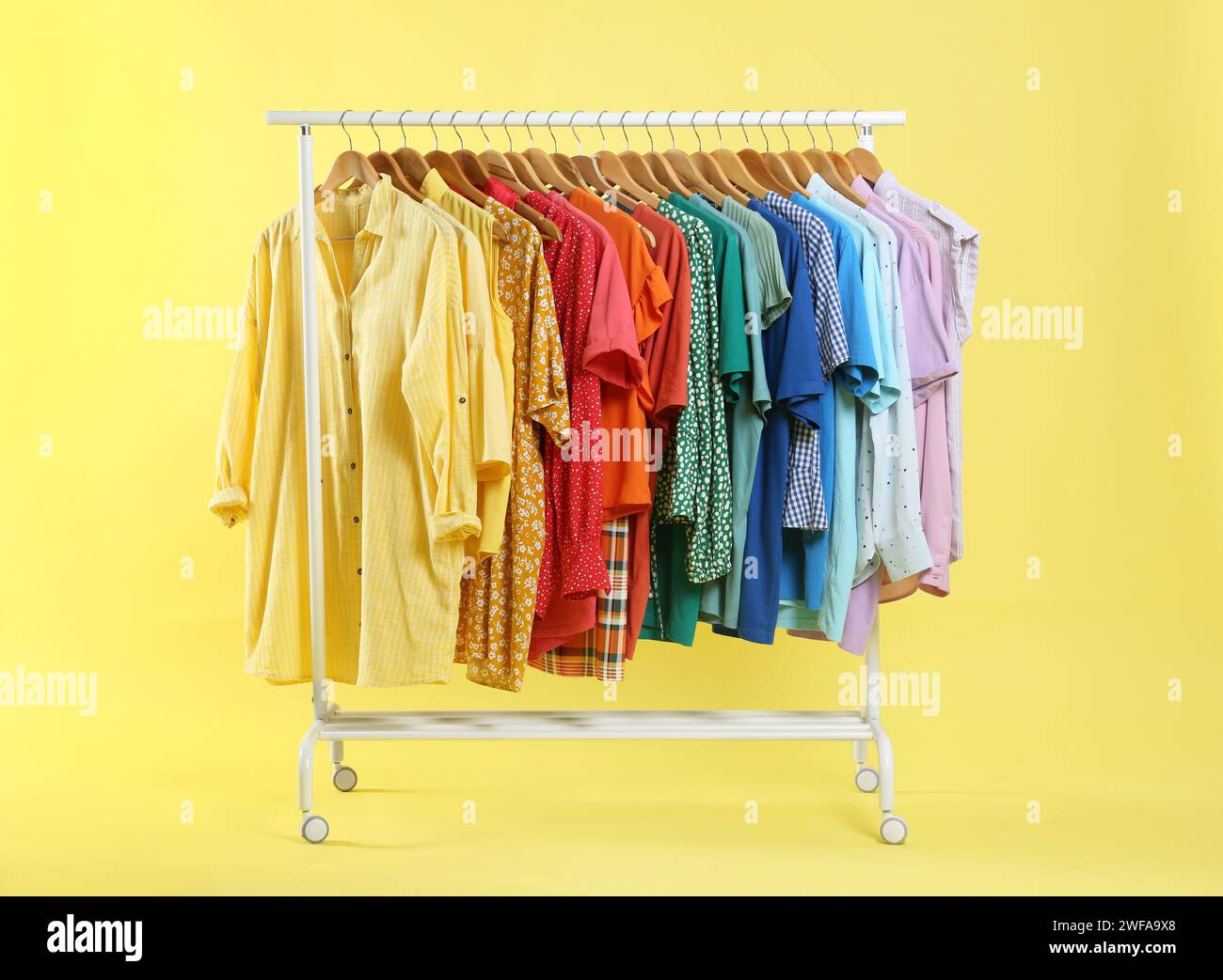 Bright clothes hanging on rack against yellow background. Rainbow ...
