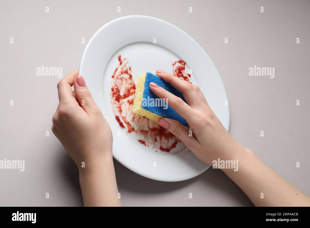 Woman washing dirty plate with sponge on light grey background, closeup ...