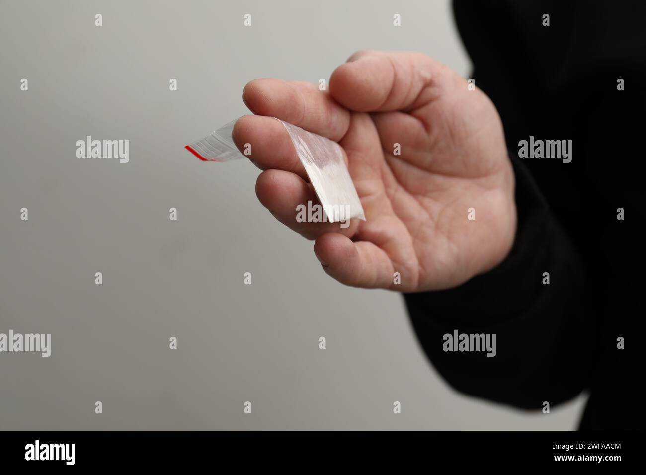 Addicted man with plastic bag of hard drug on light grey background ...