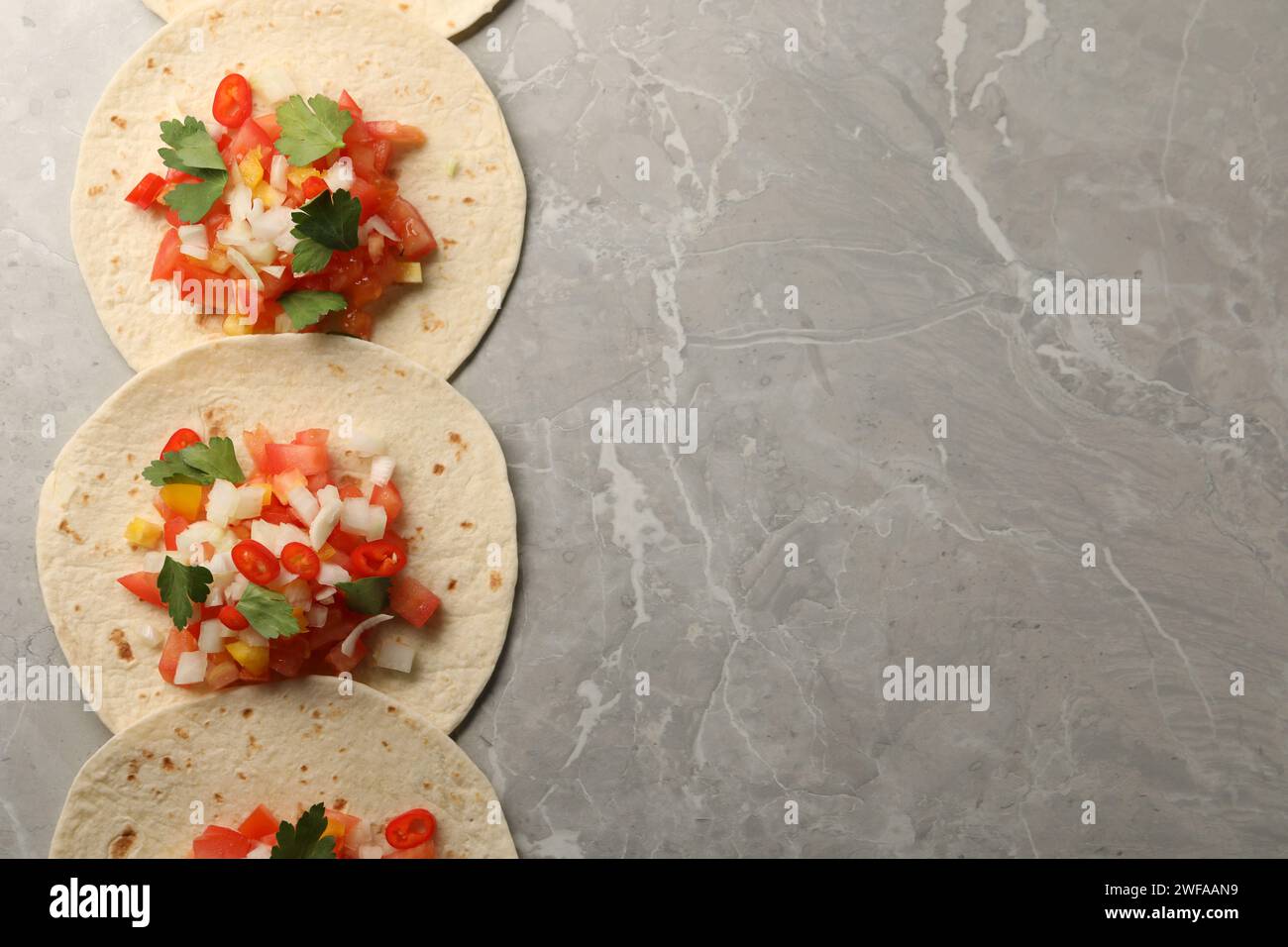 Delicious tacos with vegetables and parsley on grey marble table, top ...