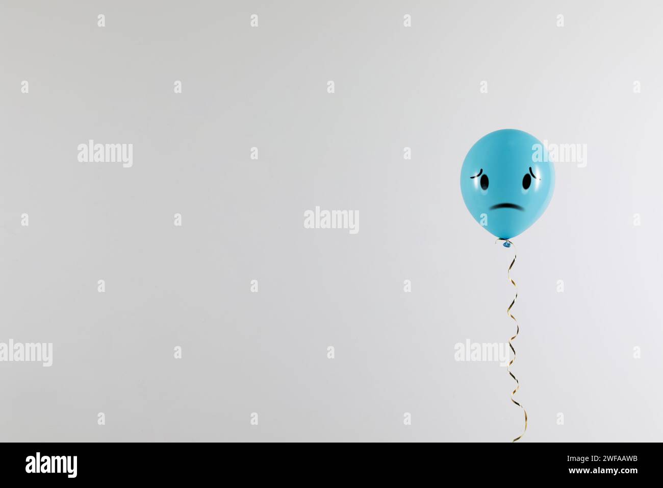 Light blue balloon with sad face on grey background. Space for text ...