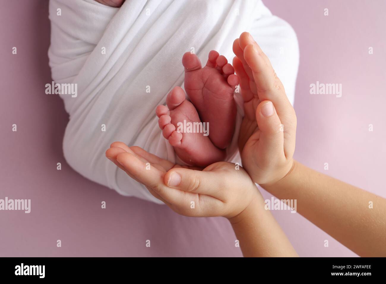 The palms of mother are holding the foot of the newborn baby in a white ...