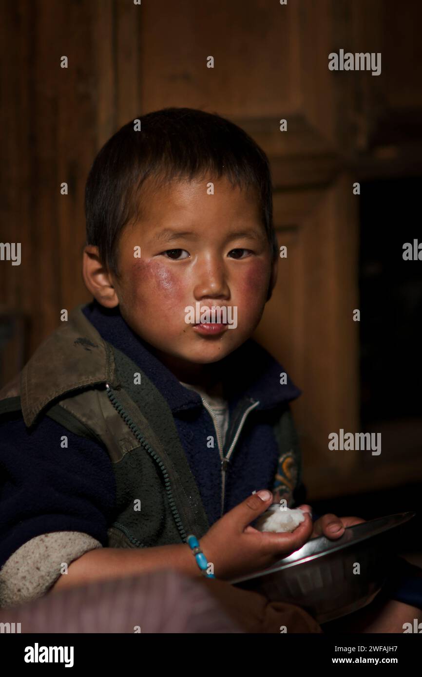Young Bhutanese boy eats red rice with his hands from a metal bowl in ...