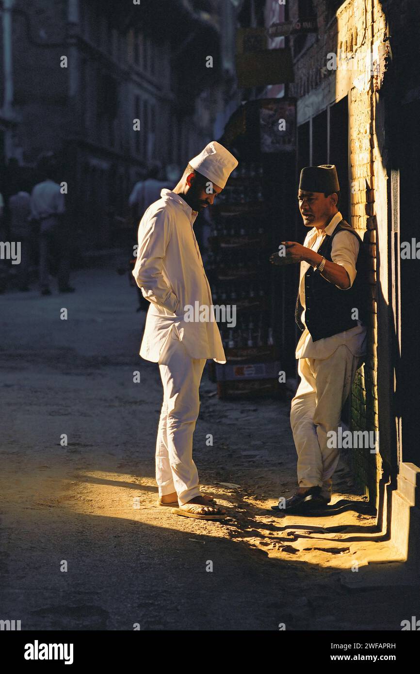 Two men chat in a patch of sunlight in a Kathmandu backstreet ...