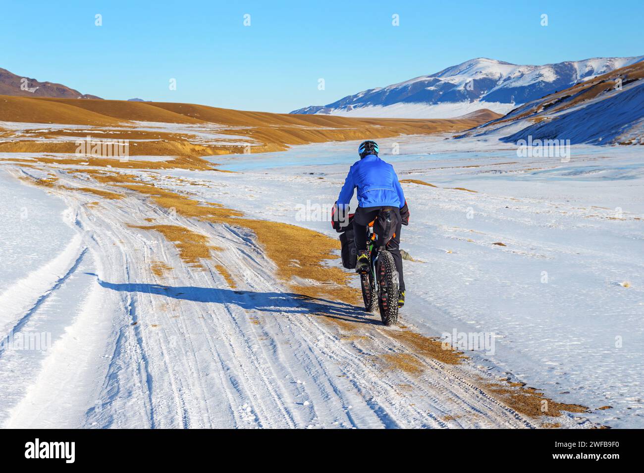 A male traveler rides a fat bike in the mountains in winter. Winter ...