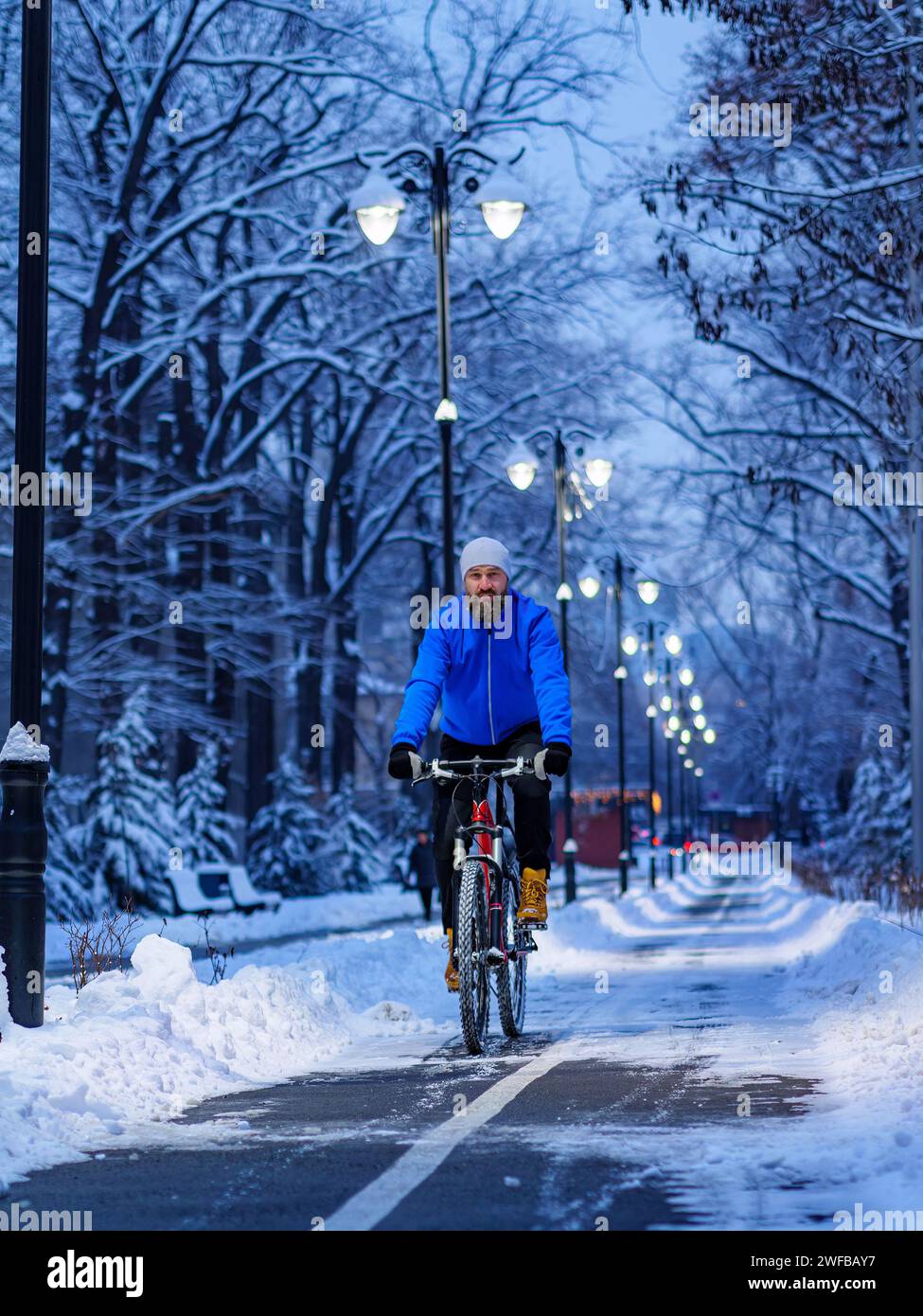 A guy rides a bicycle in the city on a winter evening along a bike path ...