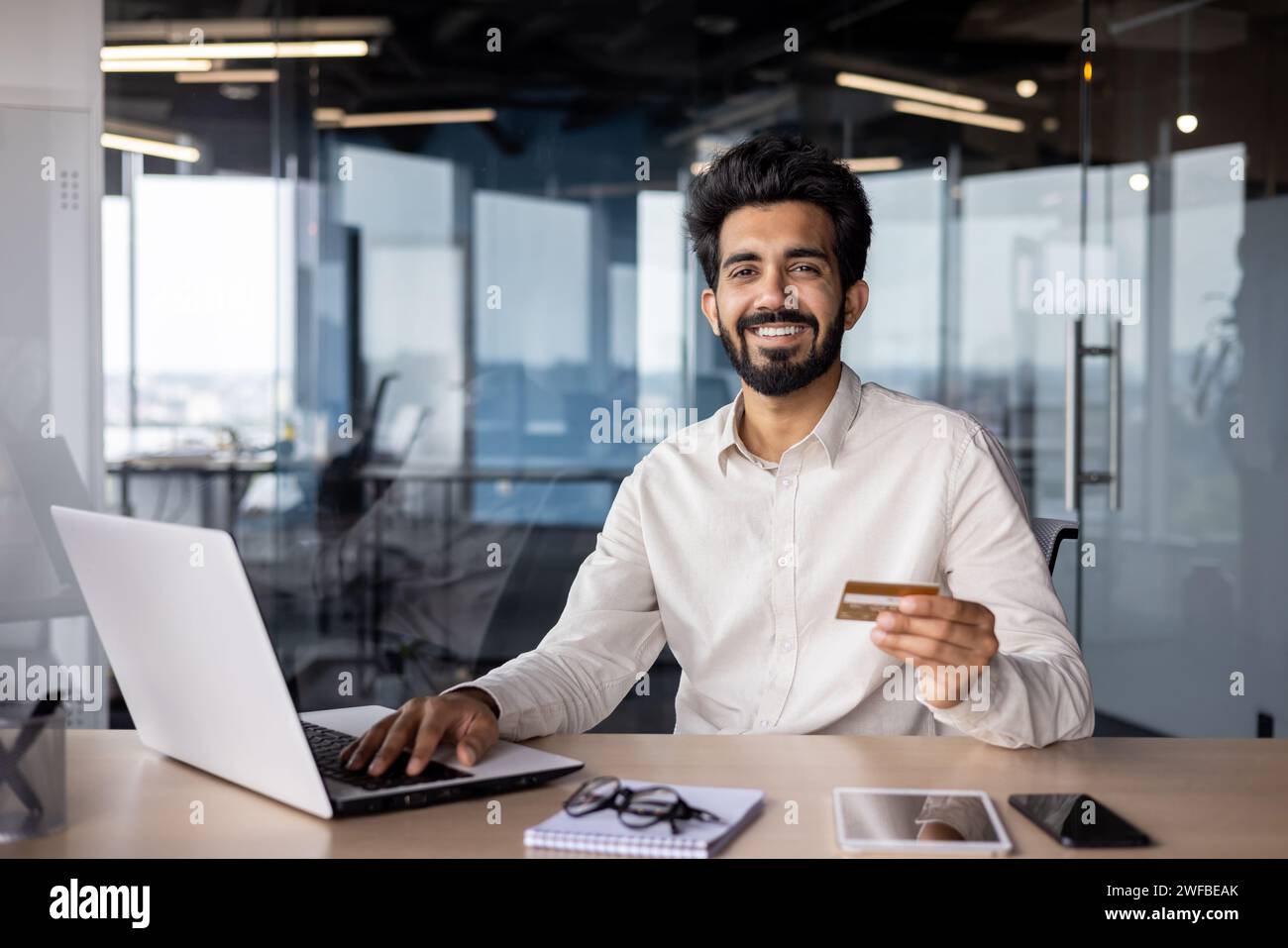 Portrait of a smiling young Indian man financier holding a credit card ...