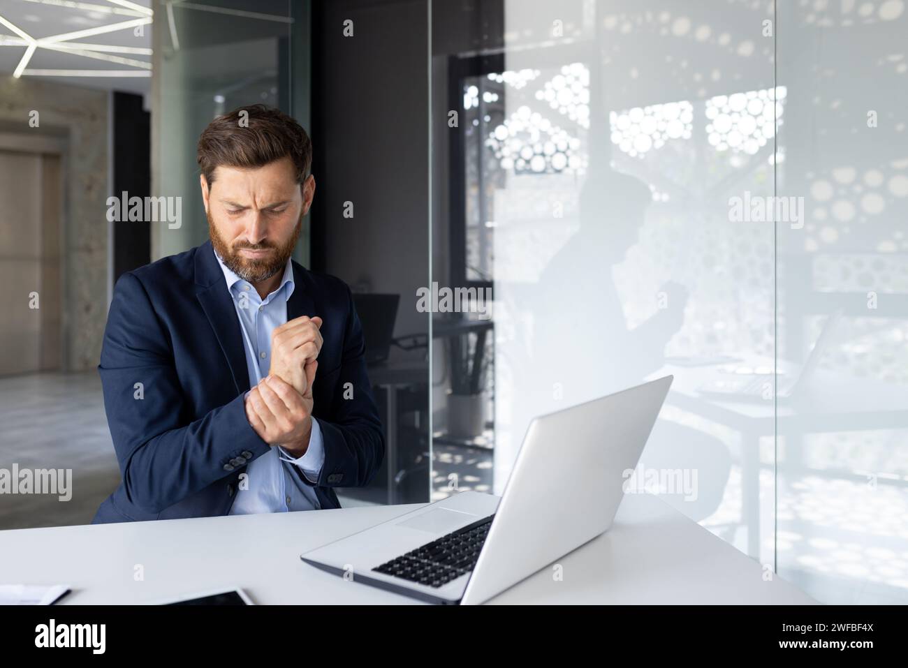 Tired young man businessman sits working in the office at the laptop ...